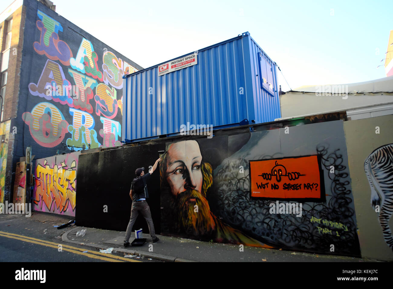man using black paint & roller to paint over graffiti wall art in ...