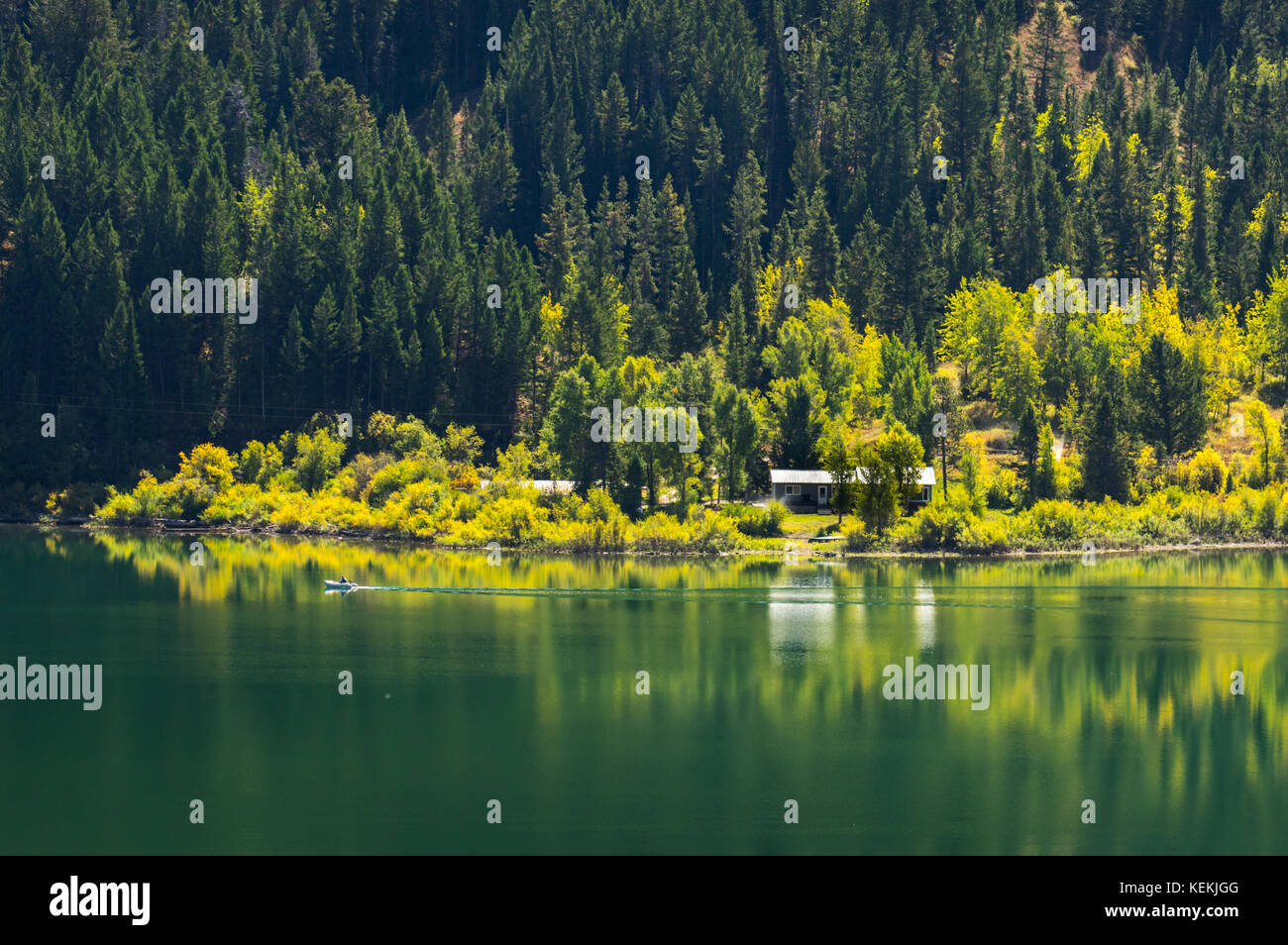 A fisherman on boat passes a small lake side home along the still ...