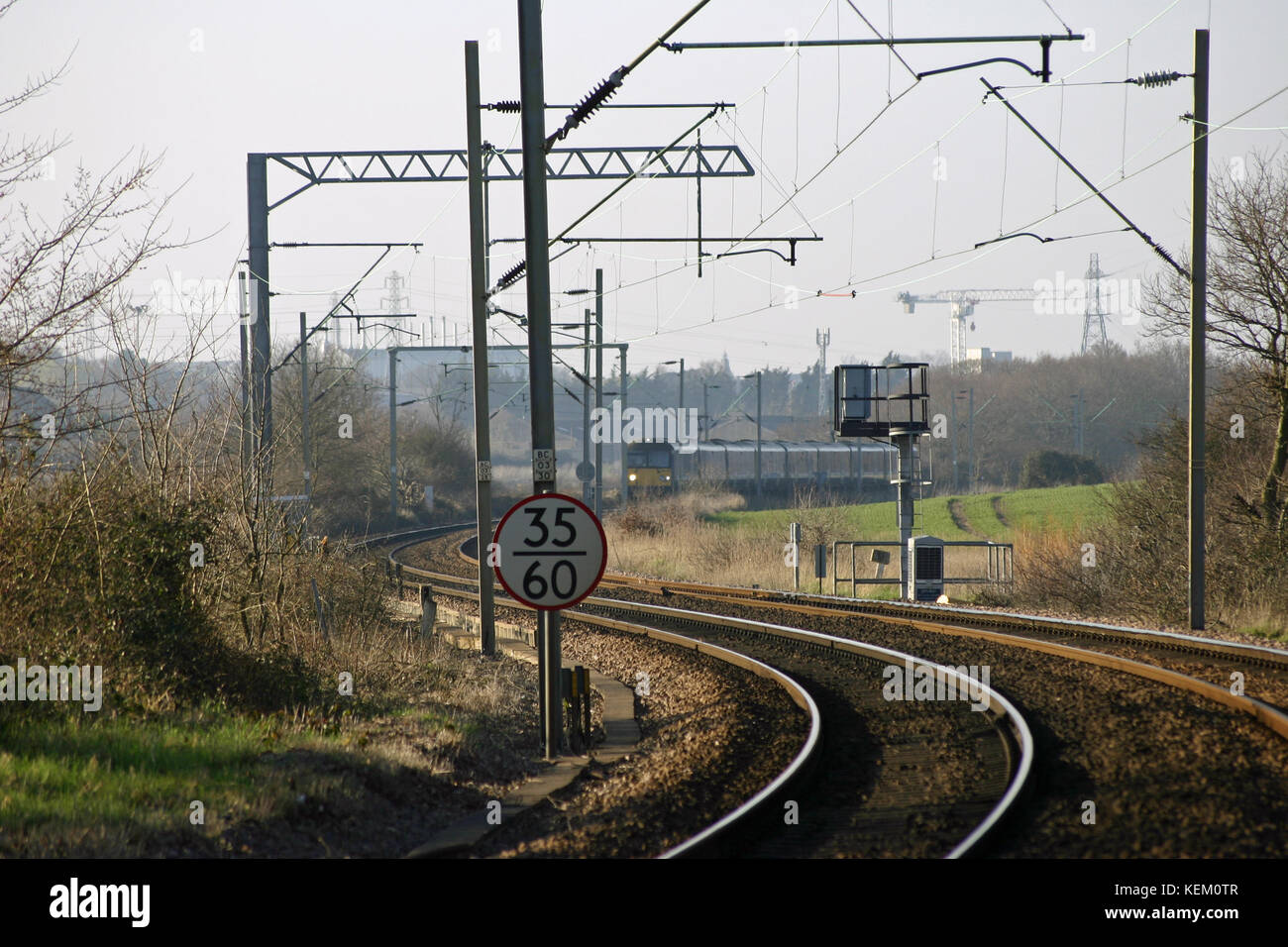 Curved local railway line with electric overhead cables and train in ...