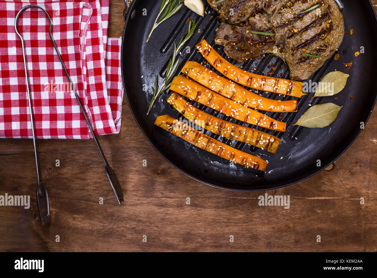 fried beef stack and fried carrots on a round frying pan, brown wooden ...