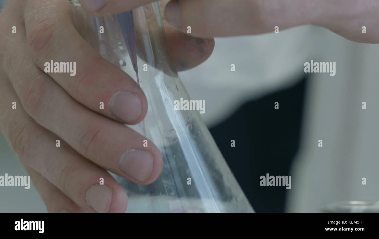 Hand pouring liquid chemicals into flask. Lab worker mixing chemicals ...