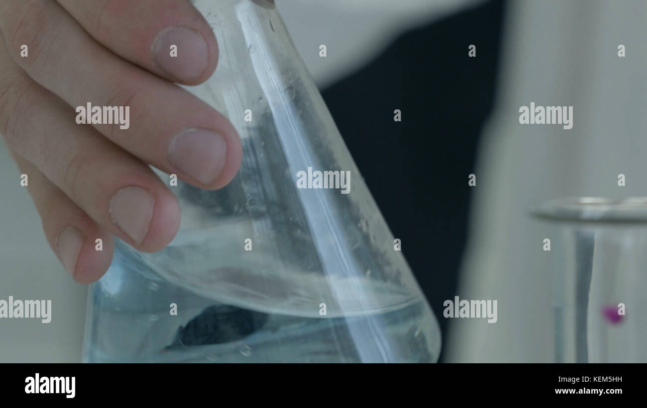 Hand pouring liquid chemicals into flask. Lab worker mixing chemicals ...