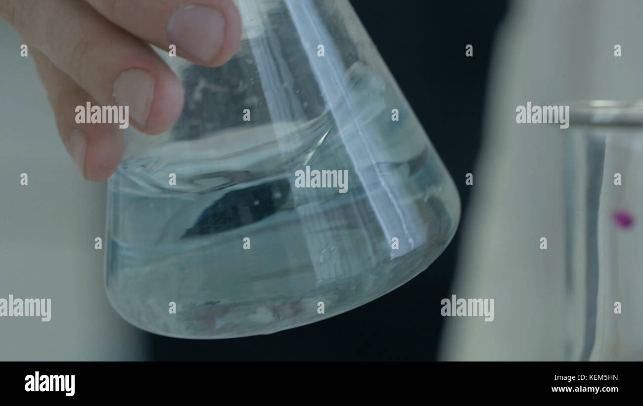 Hand pouring liquid chemicals into flask. Lab worker mixing chemicals ...