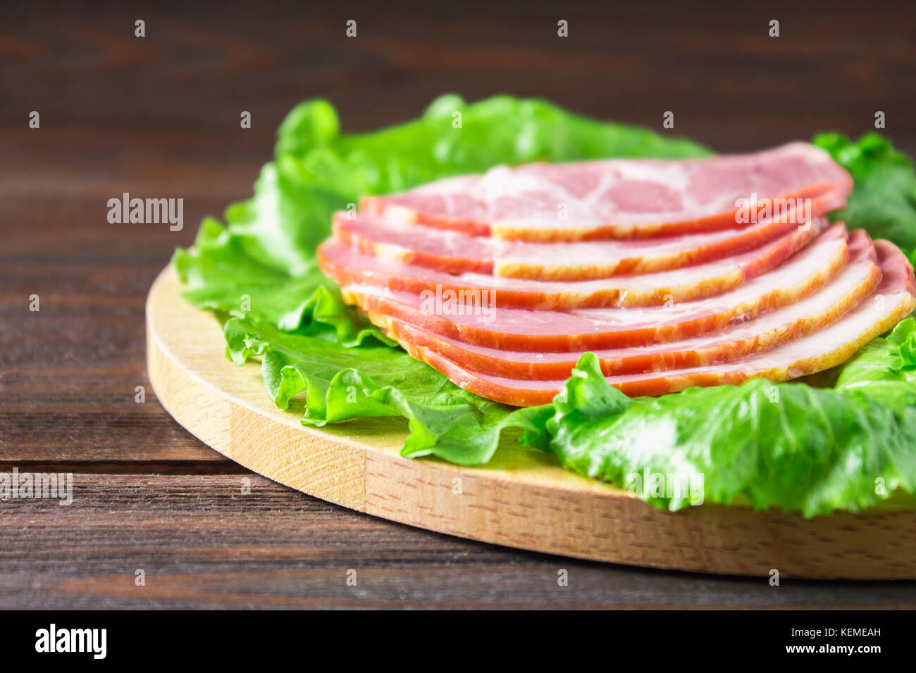 Sliced ham with fresh green lettuce leaves on a round cutting board ...