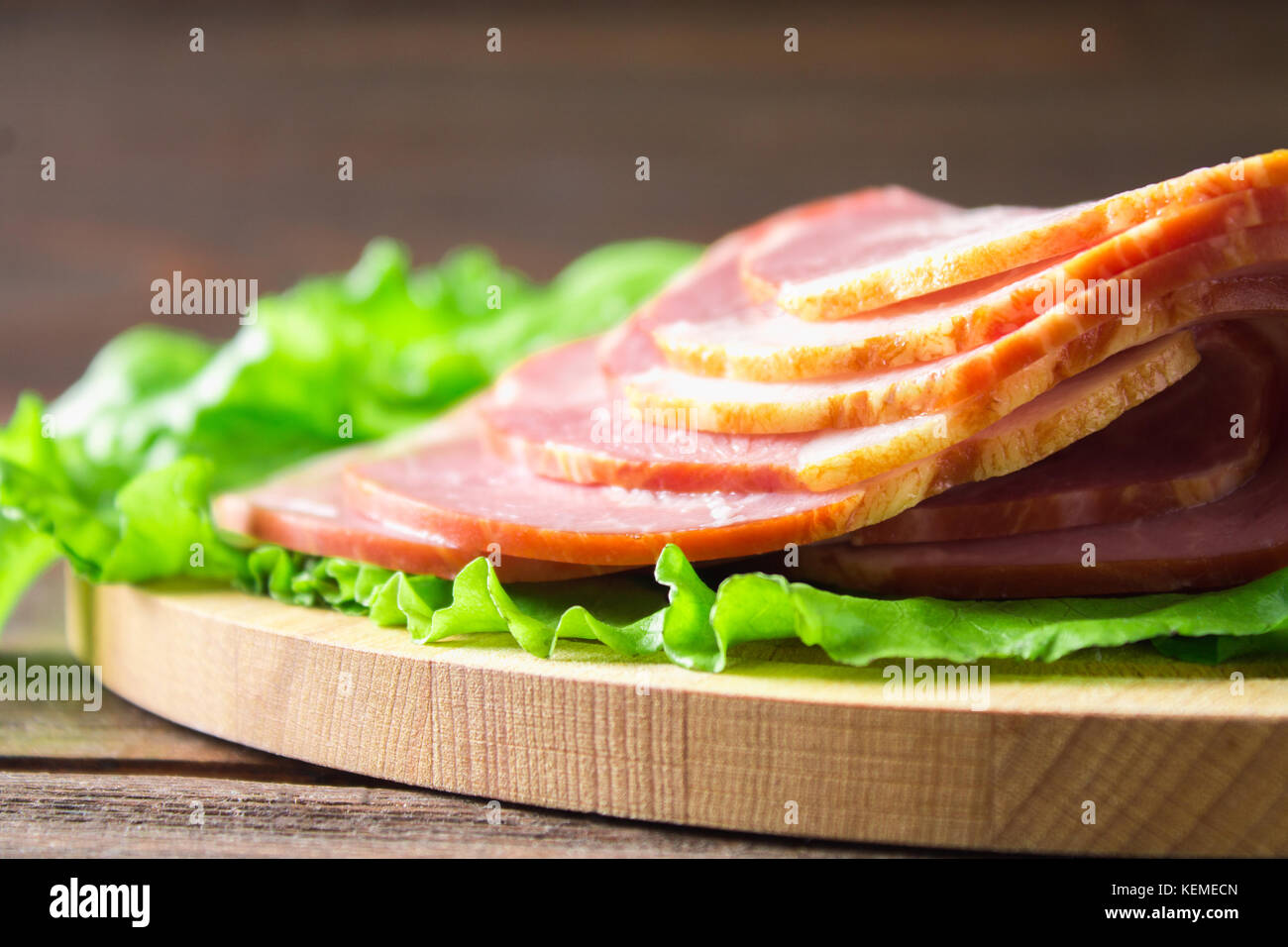 Sliced ham with fresh green lettuce leaves on a round cutting board ...