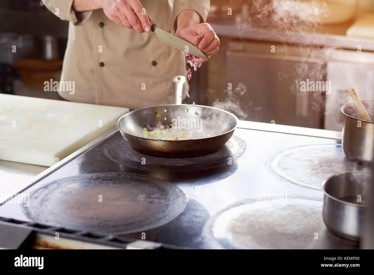 Chef cutting onion into frying pan. Male chef at professional kitchen ...