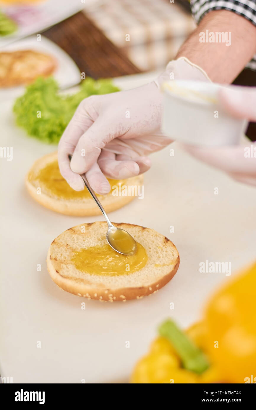 Chef hand spreading the mustard on bun for burger. Cook preparing ...