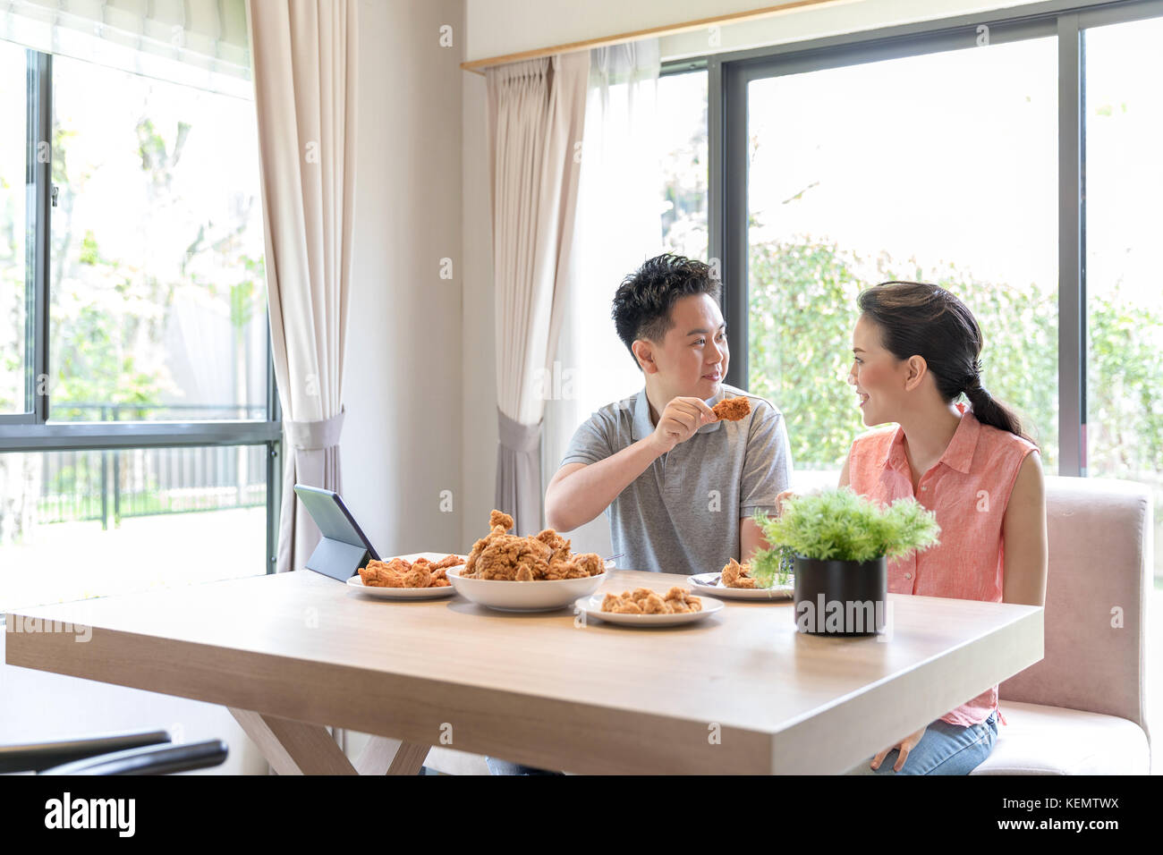 Young Asian Couples eating fried chicken together in living room of ...