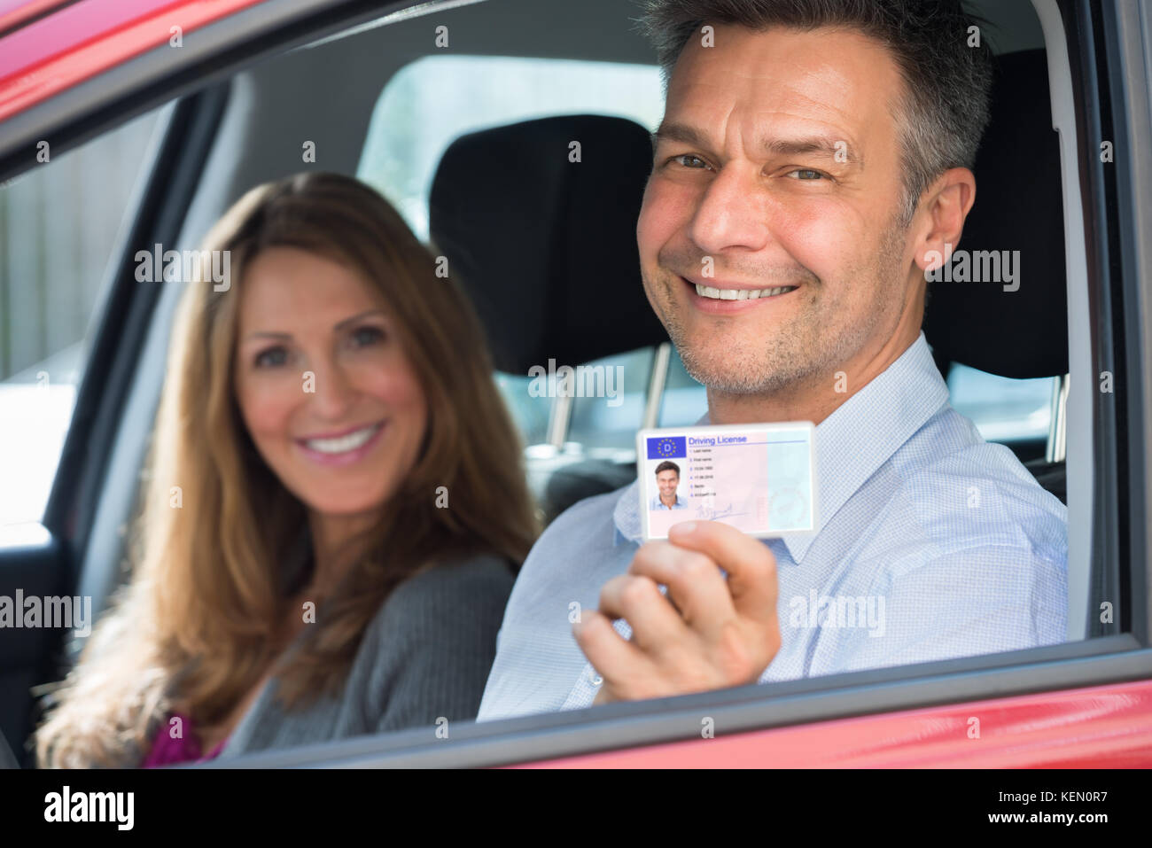 Happy Man Sitting Inside The Car With His Wife Showing Driving License ...