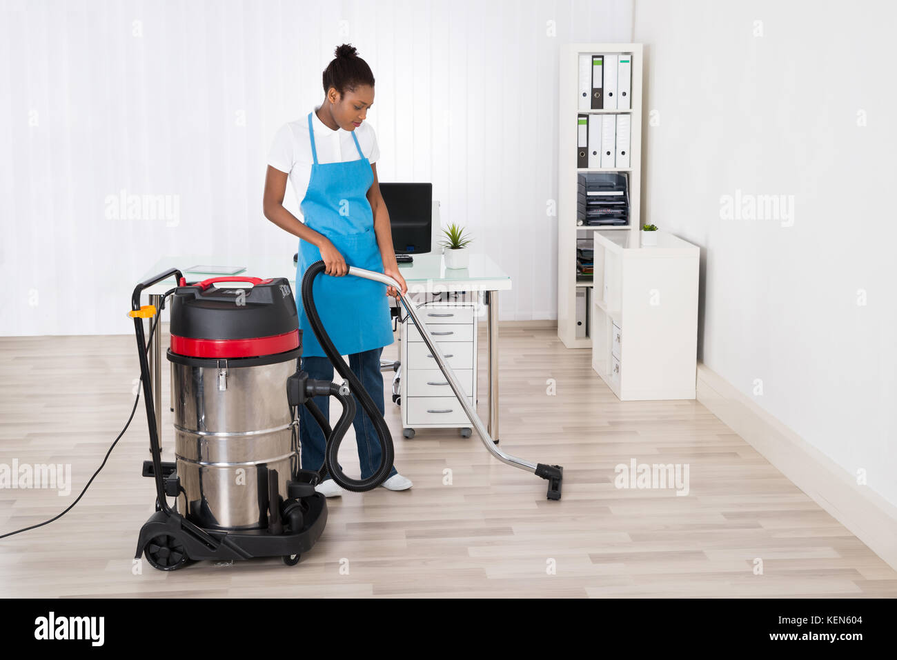 Young Female Janitor Using Vacuum Cleaner On Hardwood Floor At Office ...