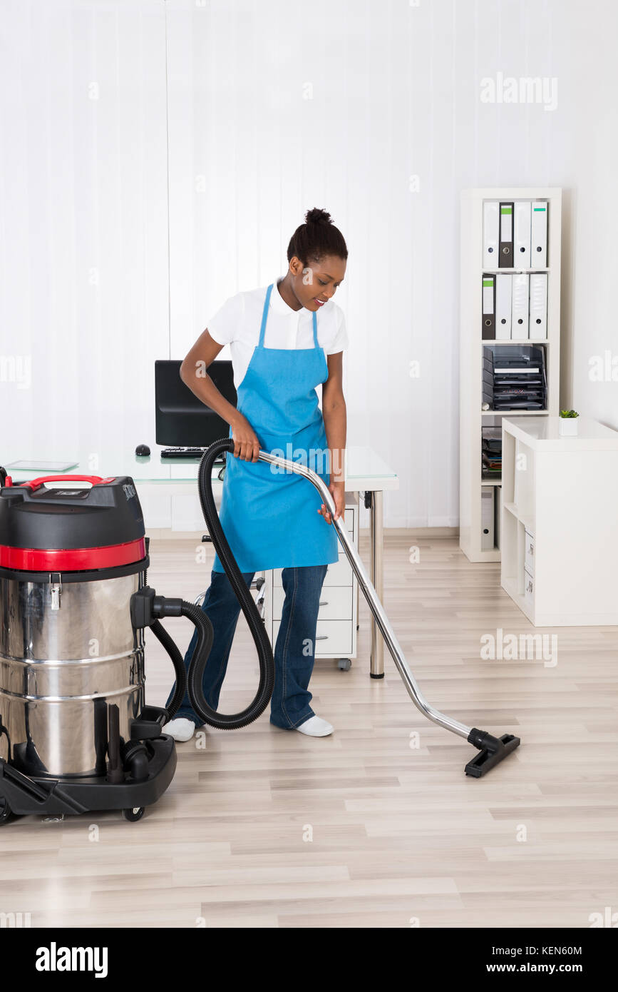Young Female Janitor Using Vacuum Cleaner On Hardwood Floor At Office ...