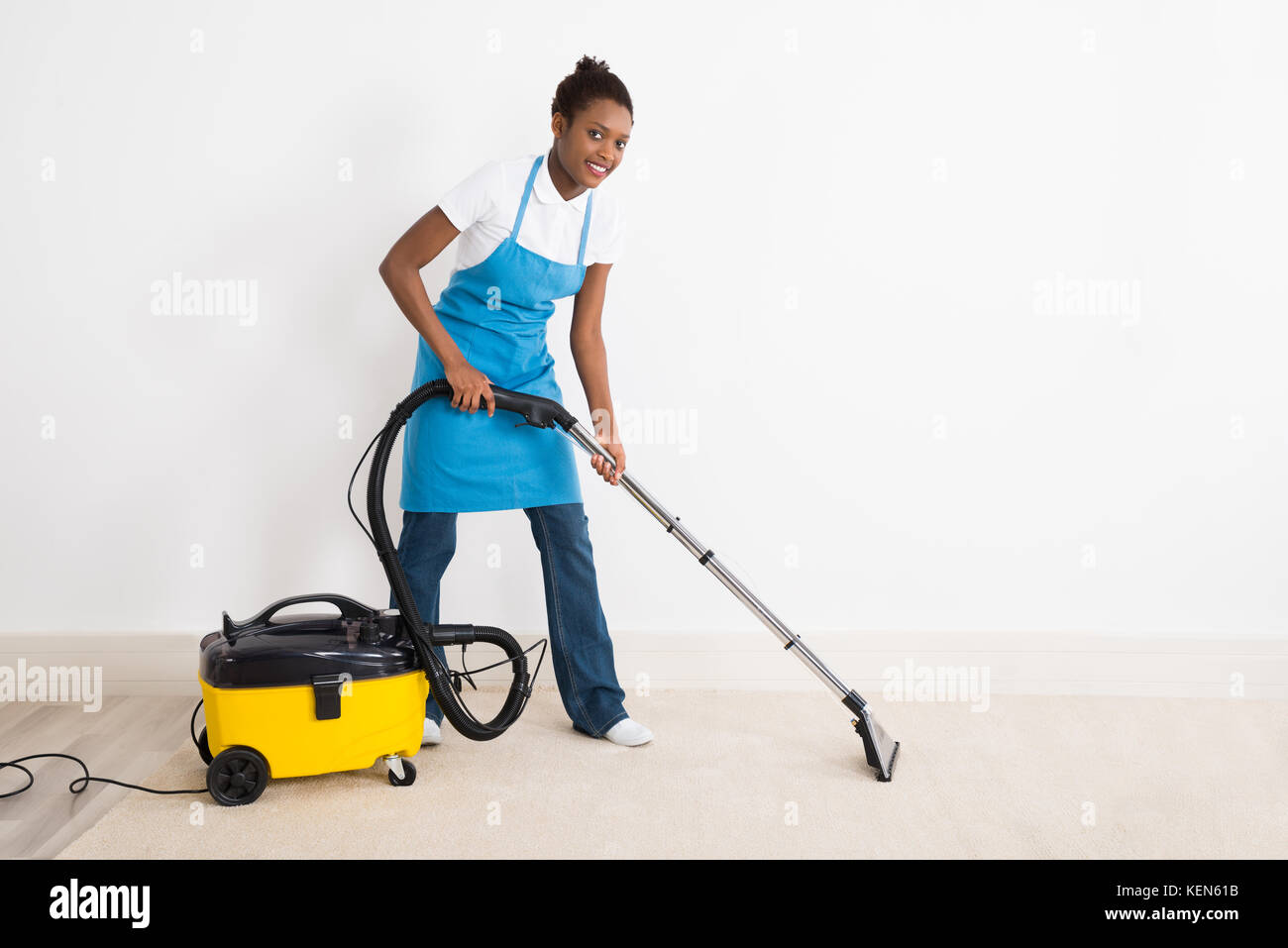 Young Happy Female Janitor Using Vacuum Cleaner On Floor At Office ...