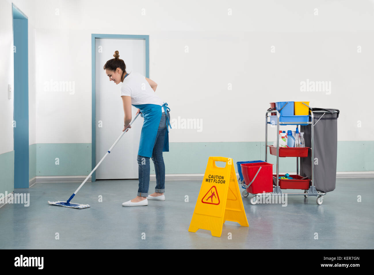Female Janitor Mopping Corridor With Caution Sign Stock Photo - Alamy