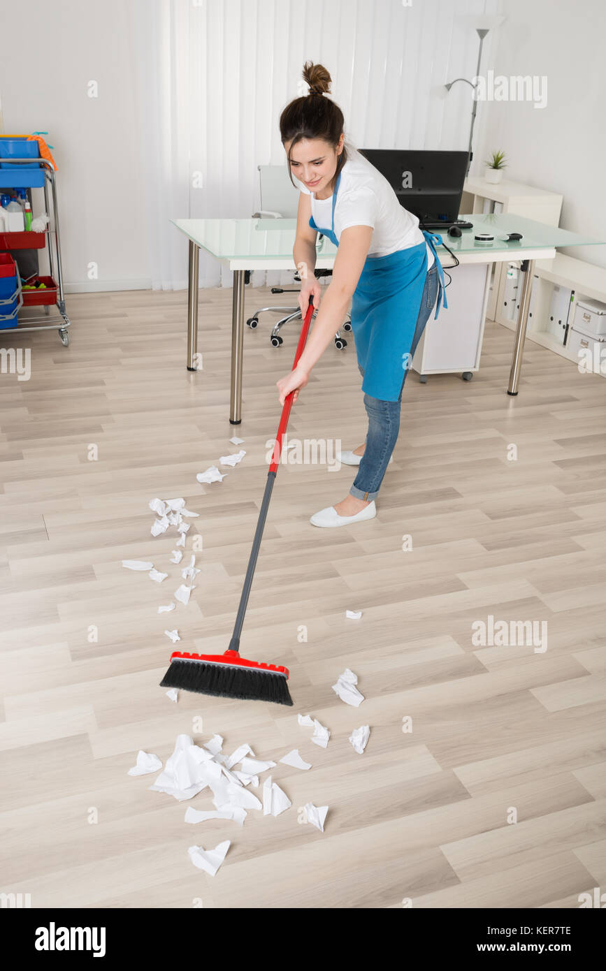 Happy Young Female Janitor Sweeping Hardwood Floor Stock Photo - Alamy