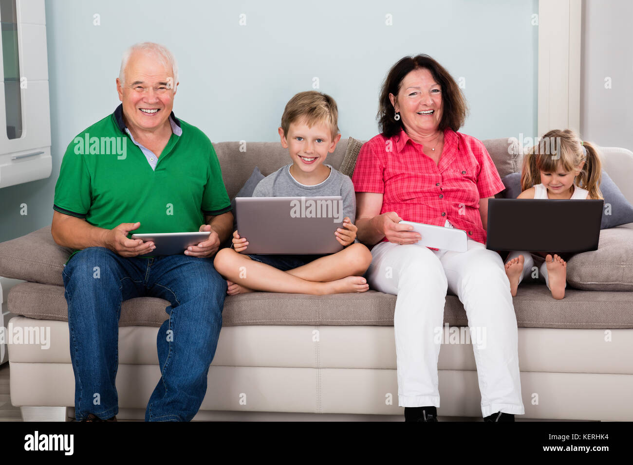 Family Sitting On Couch With Their Laptop Computers And Tablets At Home ...