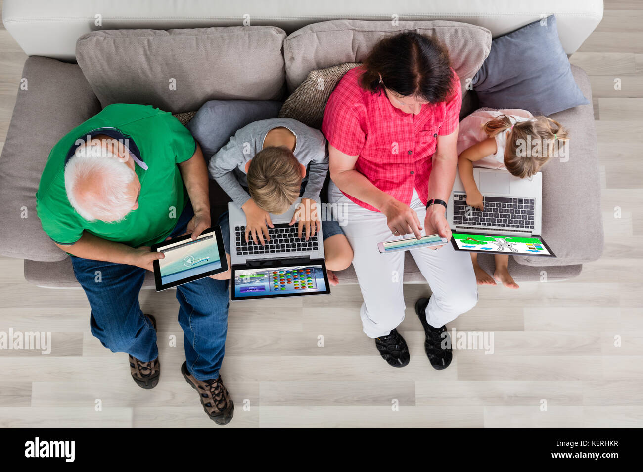 High Angle View Of Family Using Laptop Computers And Tablet On Couch At ...