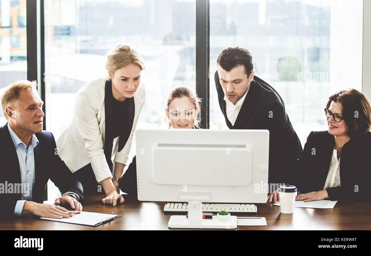 Business team look at one computer monitor having discussion in office ...