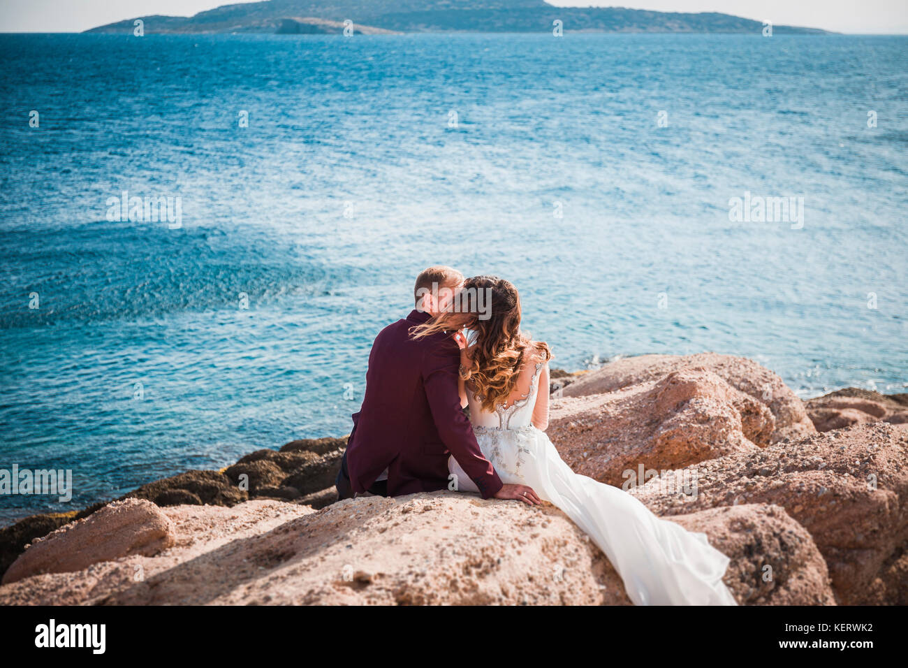 Kissing couple sitting on rock from the back Stock Photo - Alamy