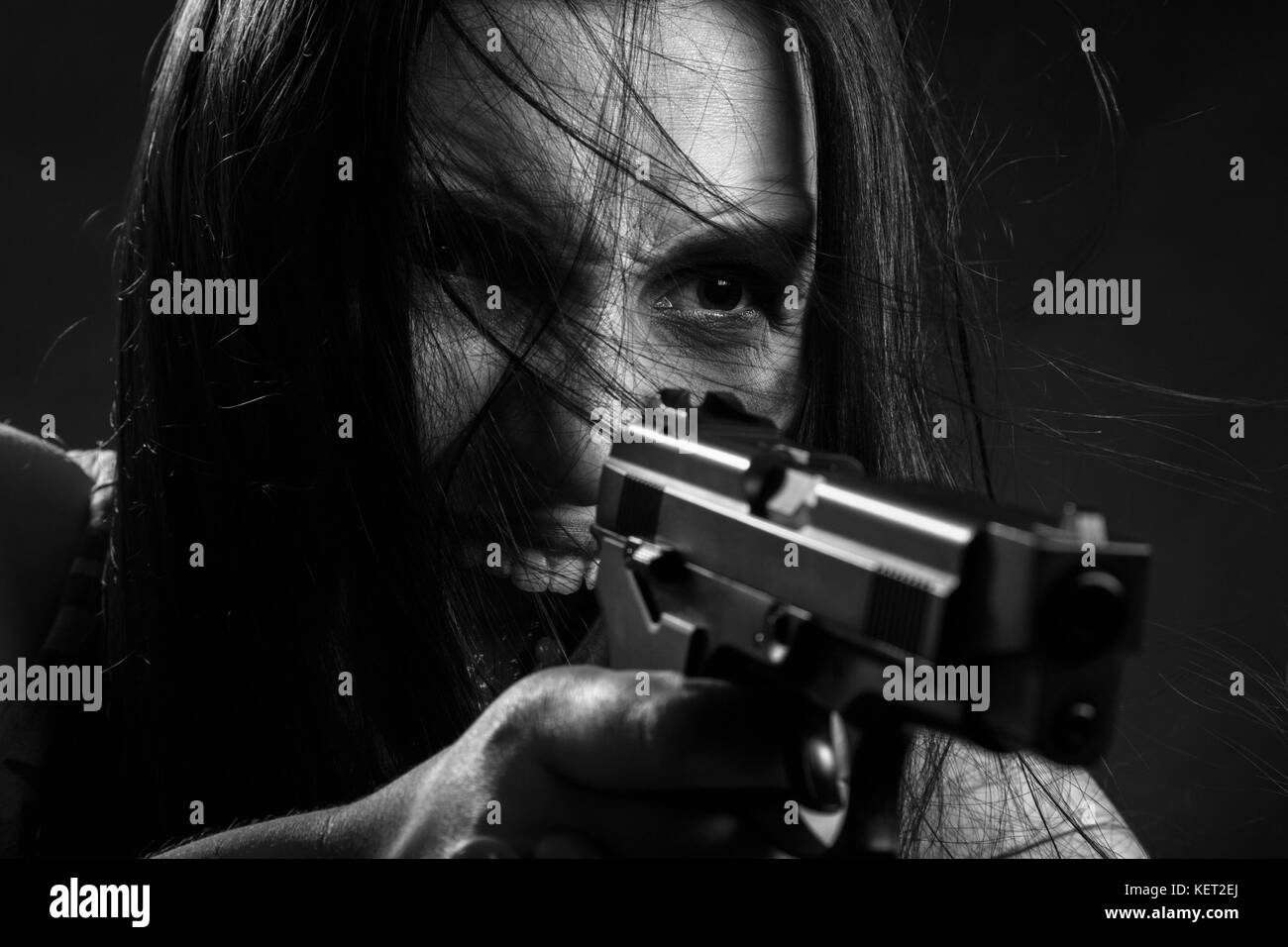screaming young woman with gun aiming on dark background, monochrome ...