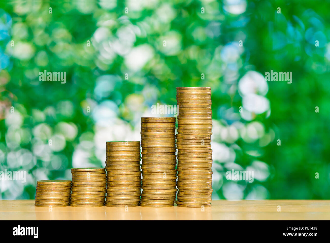 Step of coins stacks on the table in garden with green background ...