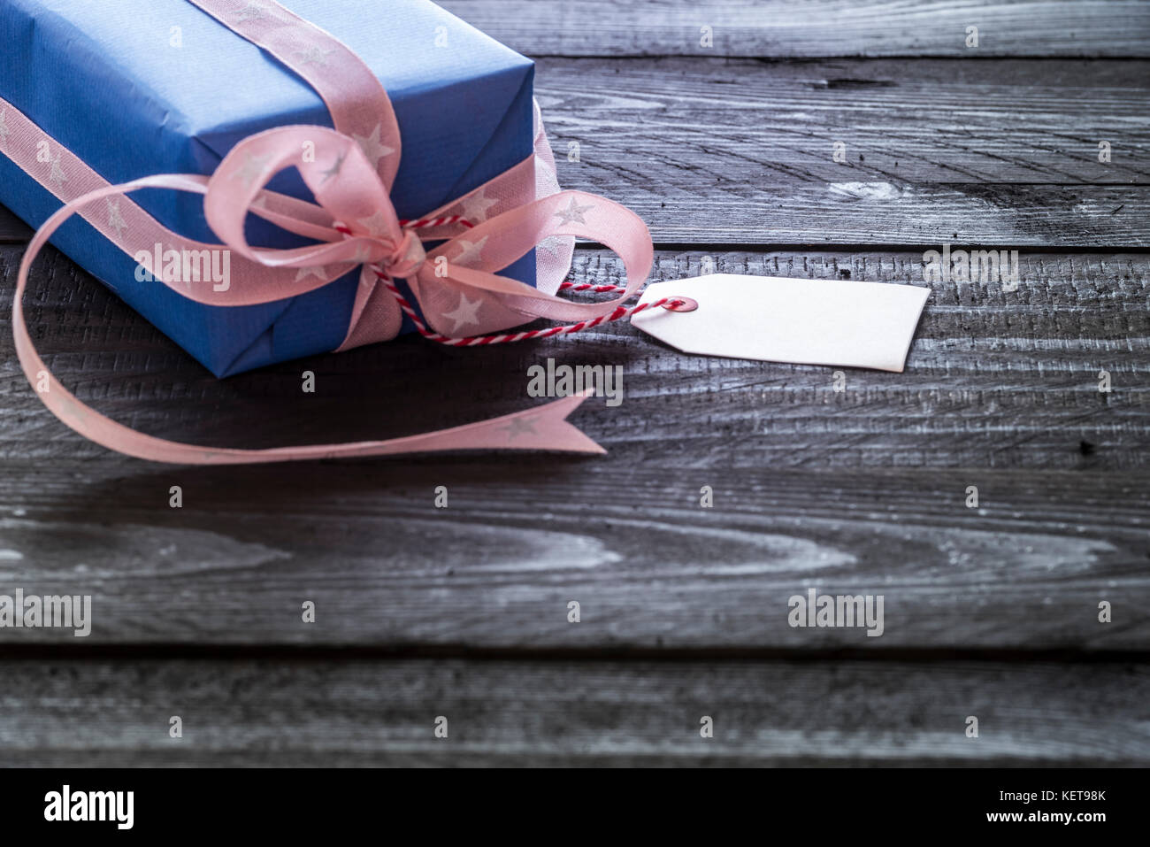 Label tag attached to gift box wrapped in blue paper tied with pink ...
