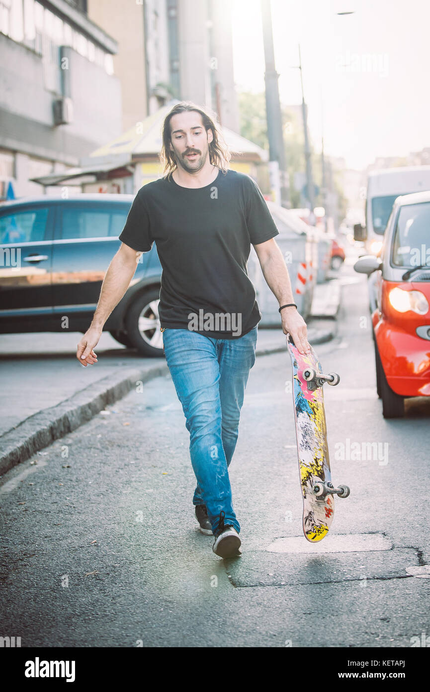 Pro skateboard rider walk down the street holding skatebord in hand ...