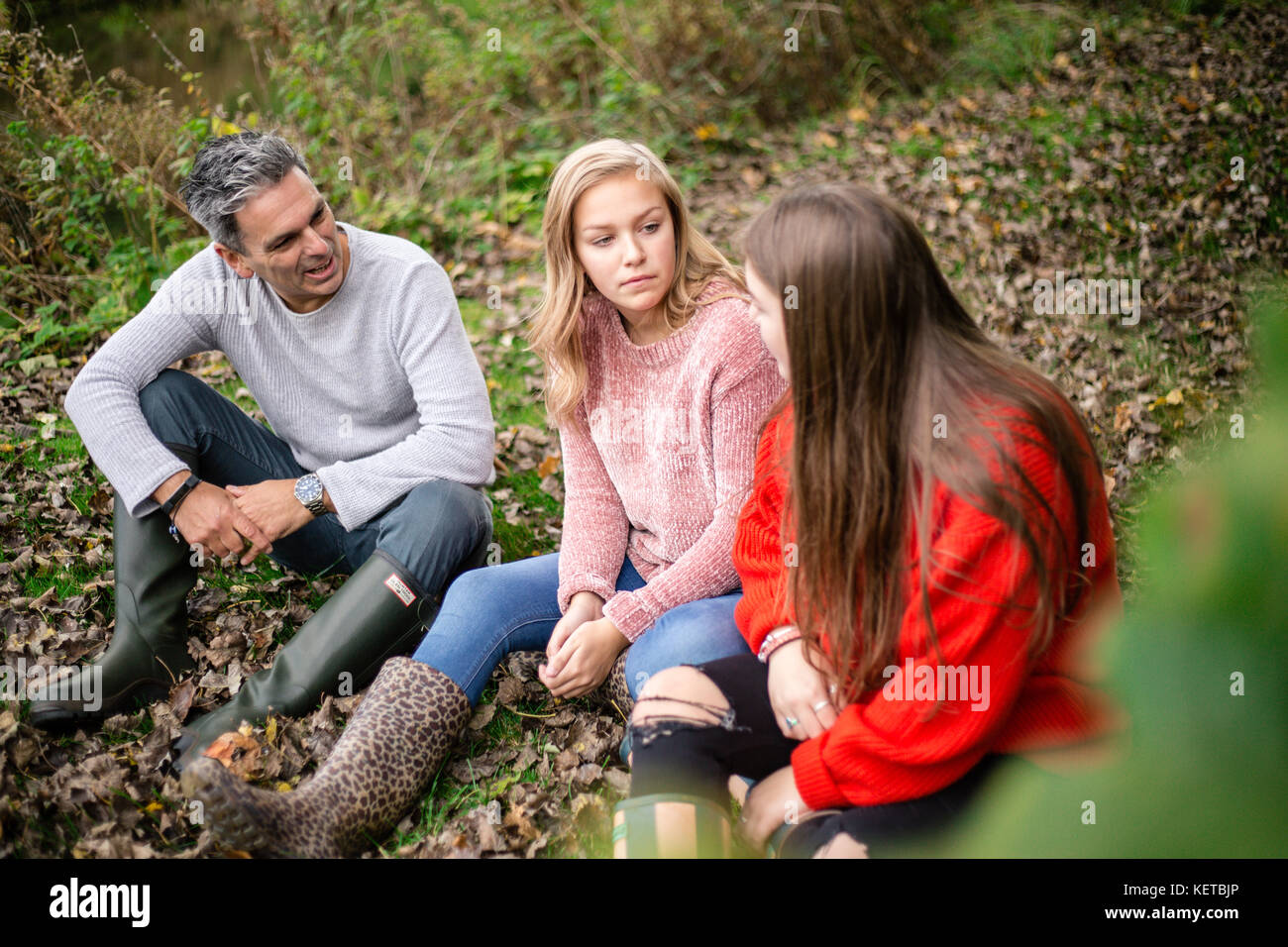 Dad sitting with two daughters talking outside in park setting Stock ...