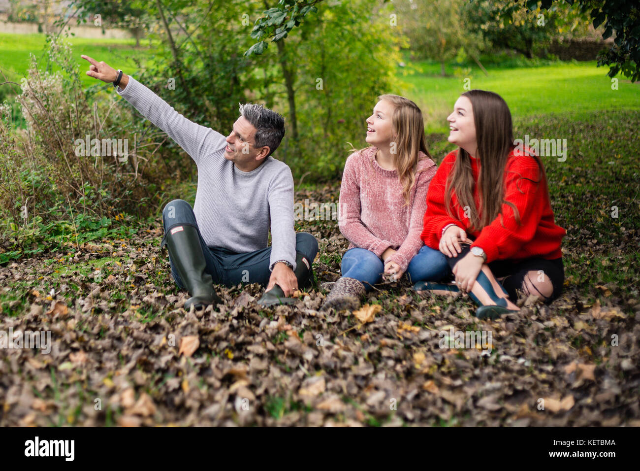 Dad sitting with two daughters talking outside in park setting Stock ...