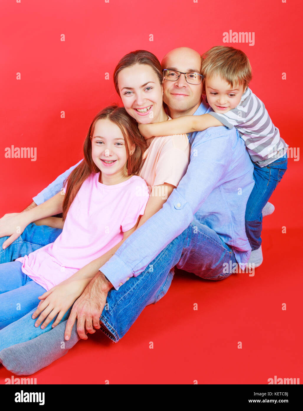 two happy young parents with two kids, isolated against red background ...