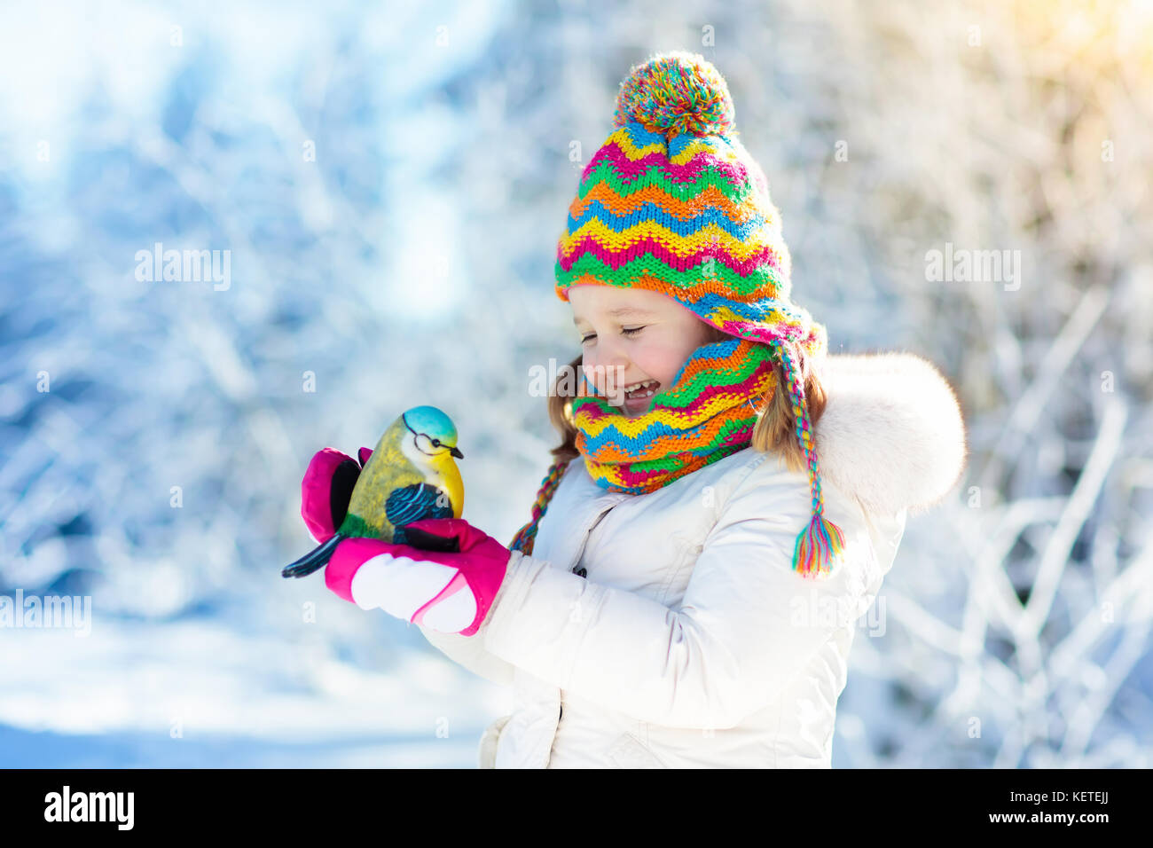 Child feeding tit bird in winter park. Kids feed birds in snowy forest ...