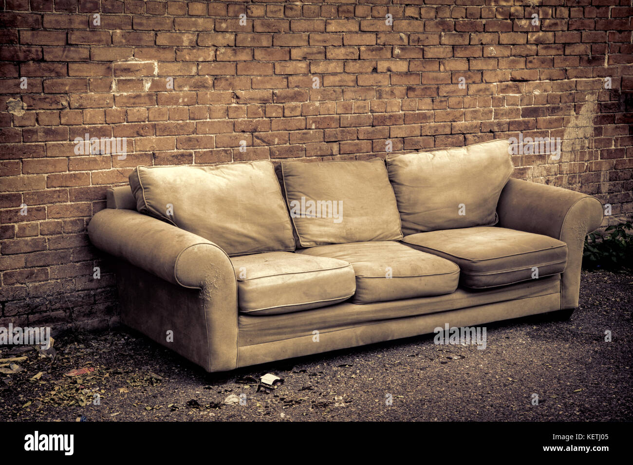 old sofa discarded in an alley, surrounded by trash and broken glass ...