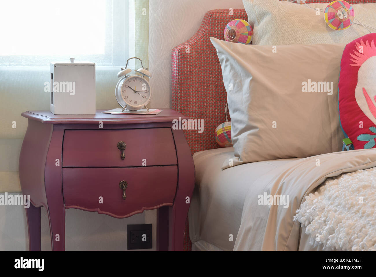 white alarm clock on bedside table and colorful pillows in modern kid ...