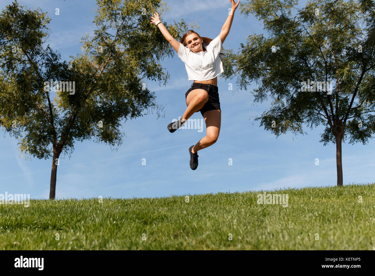 Young girl giving a joy jump in the green field with the blue sky ...