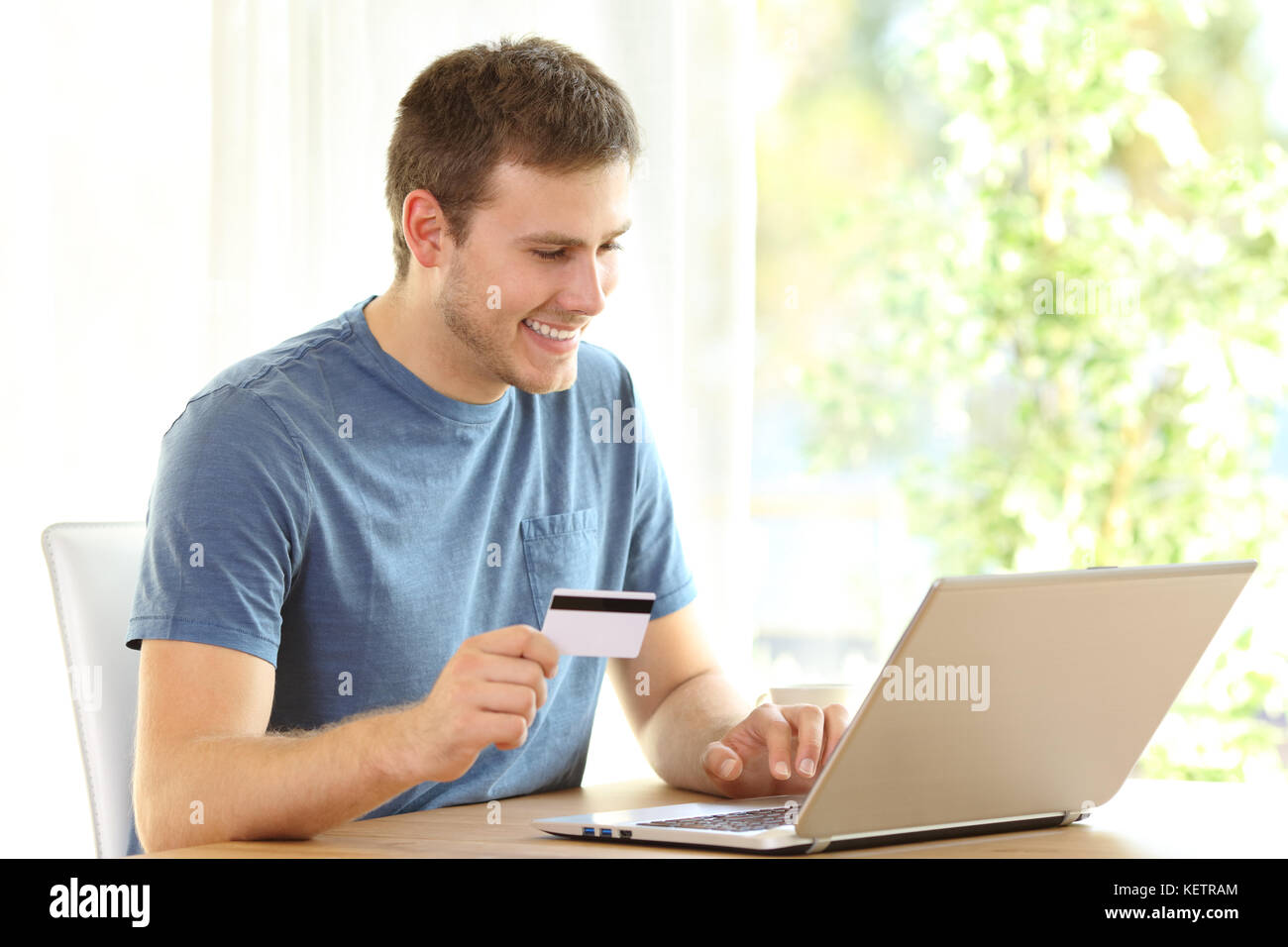 Man paying on line with credit card and a laptop on a desk at home ...
