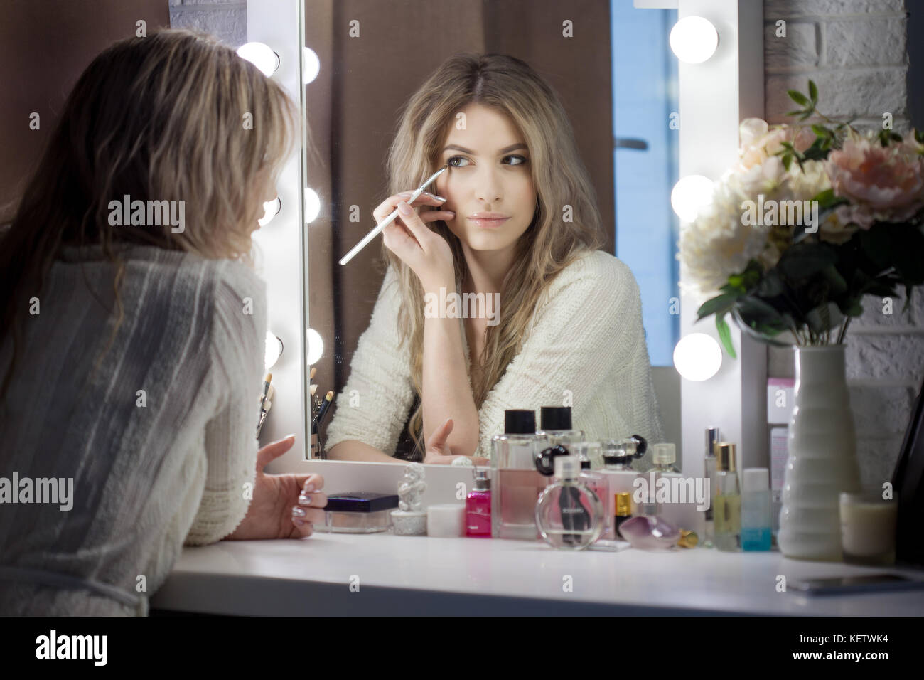 Amazing young woman doing her makeup in front of mirror. Portrait of ...