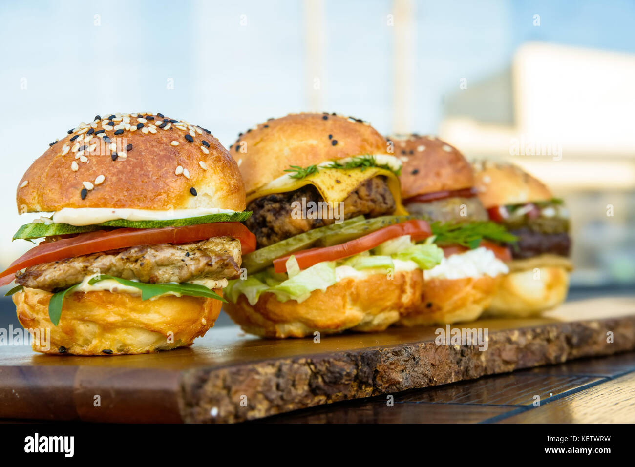 Four burgers on wooden board in restaurant Stock Photo - Alamy