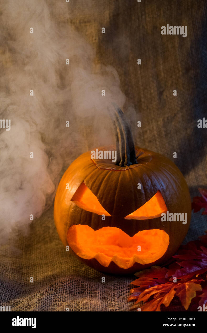 Scary jack-o-lantern, light inside and red leaves Stock Photo - Alamy