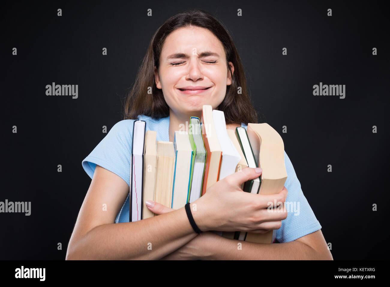 Exhausted girl student holding books in her arms and crying on dark ...