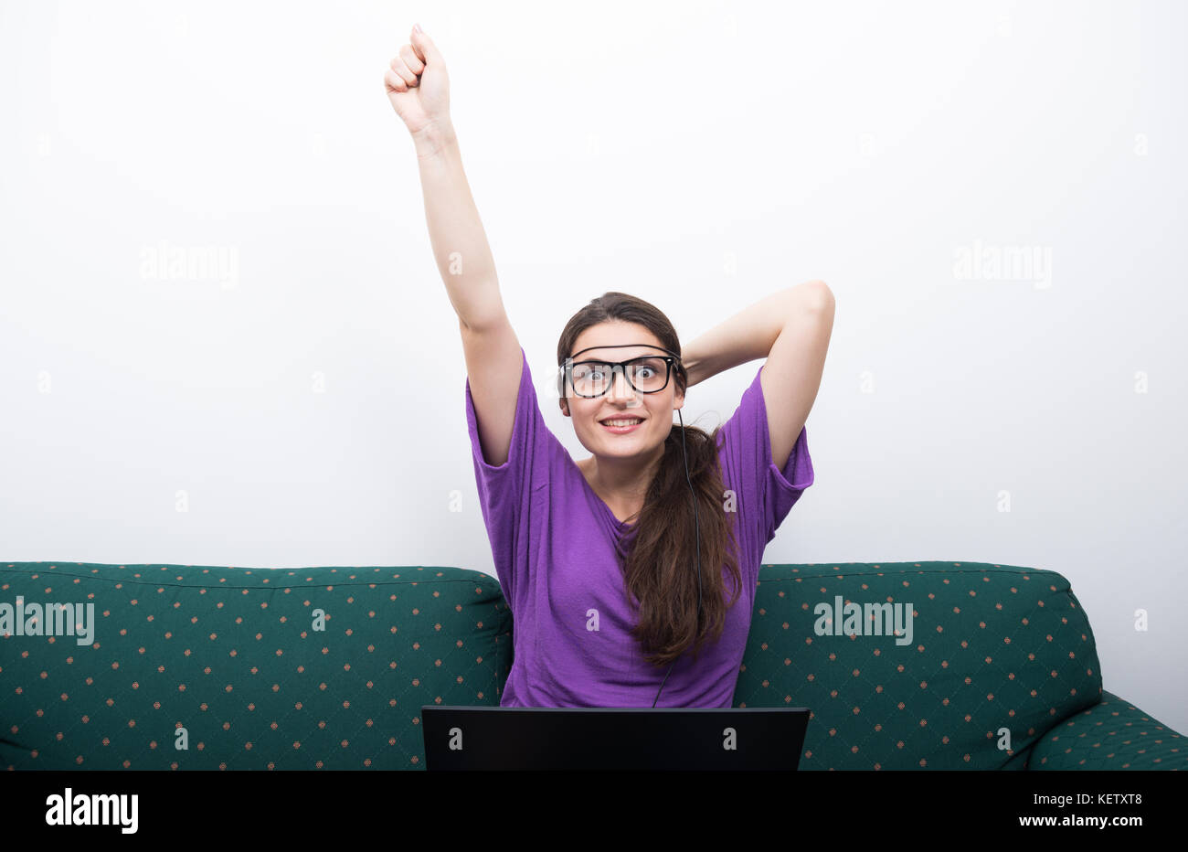 Happy young woman on the sofa with a laptop on her legs acting like a ...