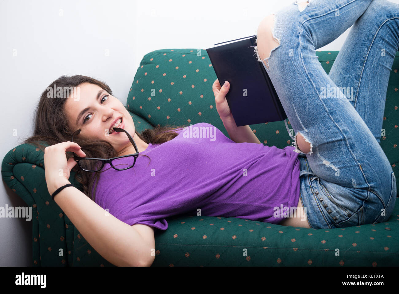 Beautiful woman reading a book lying comfortably on her back on a couch ...