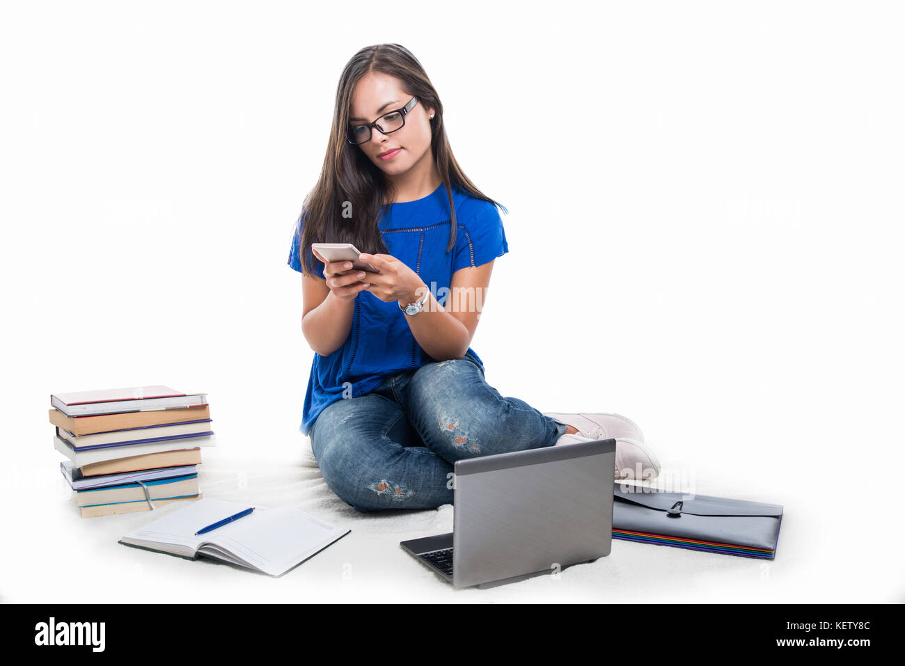 Student girl sitting texting on smartphone with books and laptop around ...