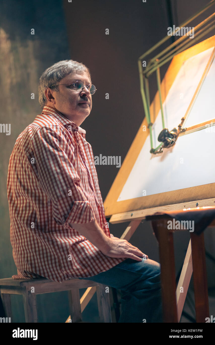 The mature creative engineer working with project on drawing board ...