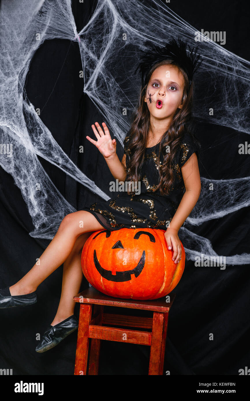 Cute little witch sitting on the pumpkin on background with a cobweb ...