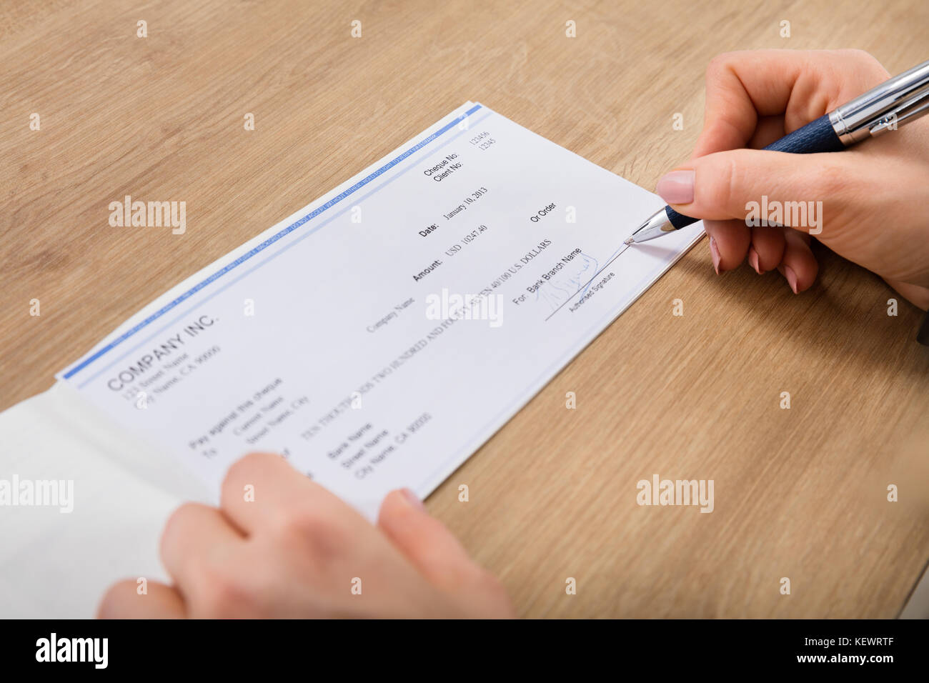 Close-up Of A Person Hand Signing Cheque At Wooden Desk Stock Photo - Alamy