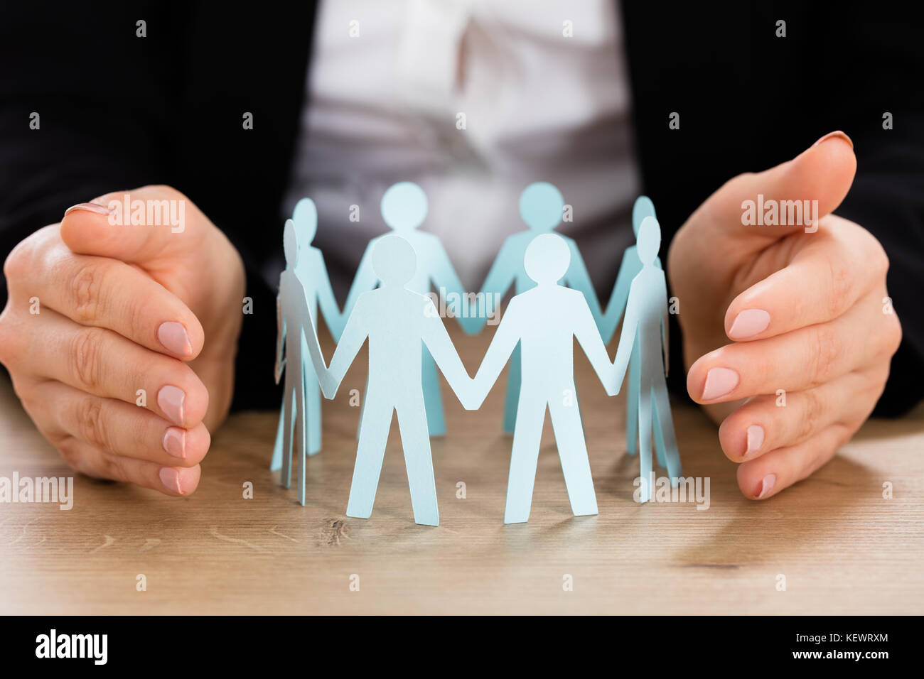 Close-up Of Businesswoman Hand Protecting Cut-out Figures On Desk In ... Close-up Of Businesswoman Hand Protecting Cut-out Figures On Desk In ...