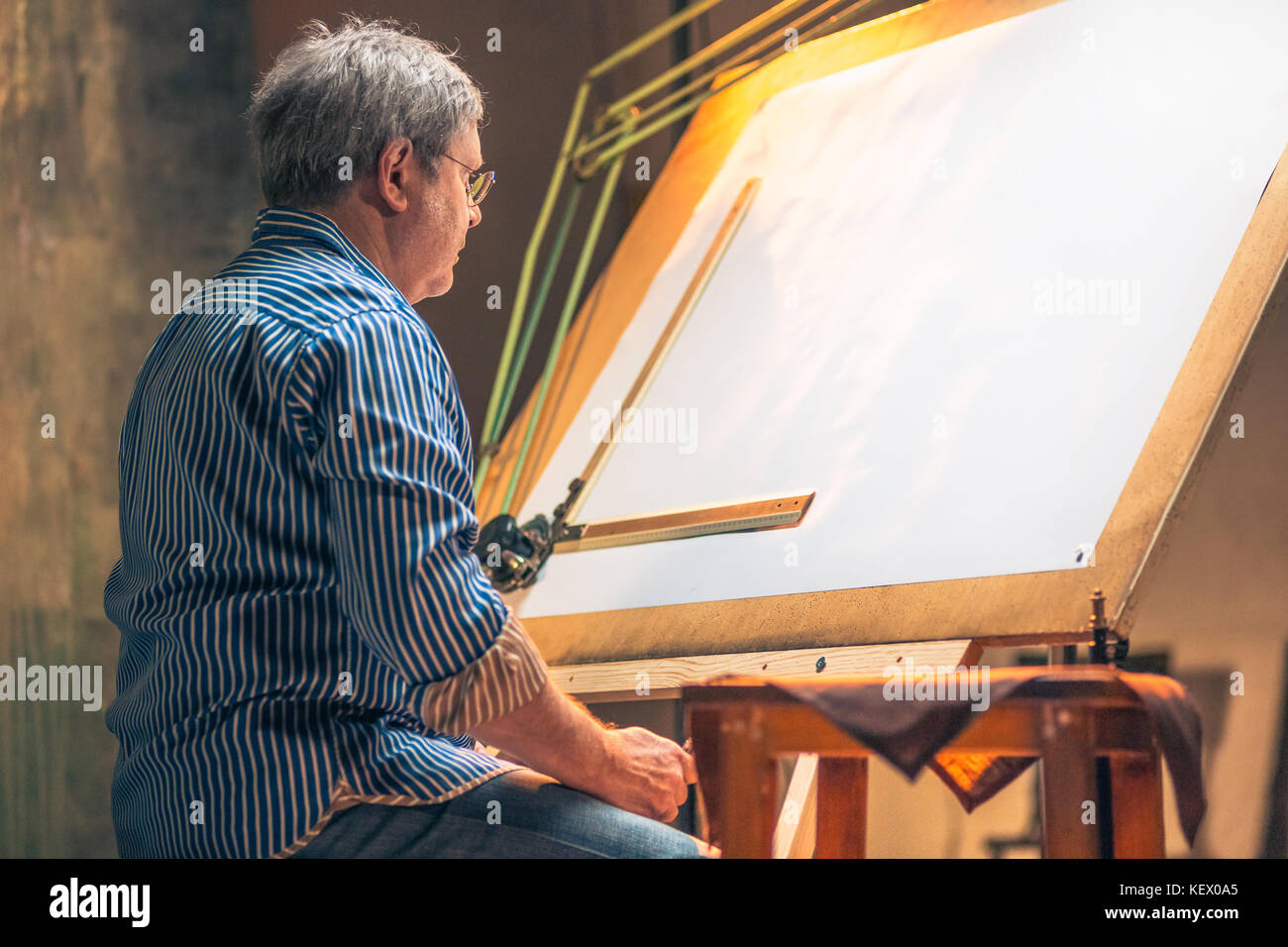 The mature creative engineer working with project on drawing board ...