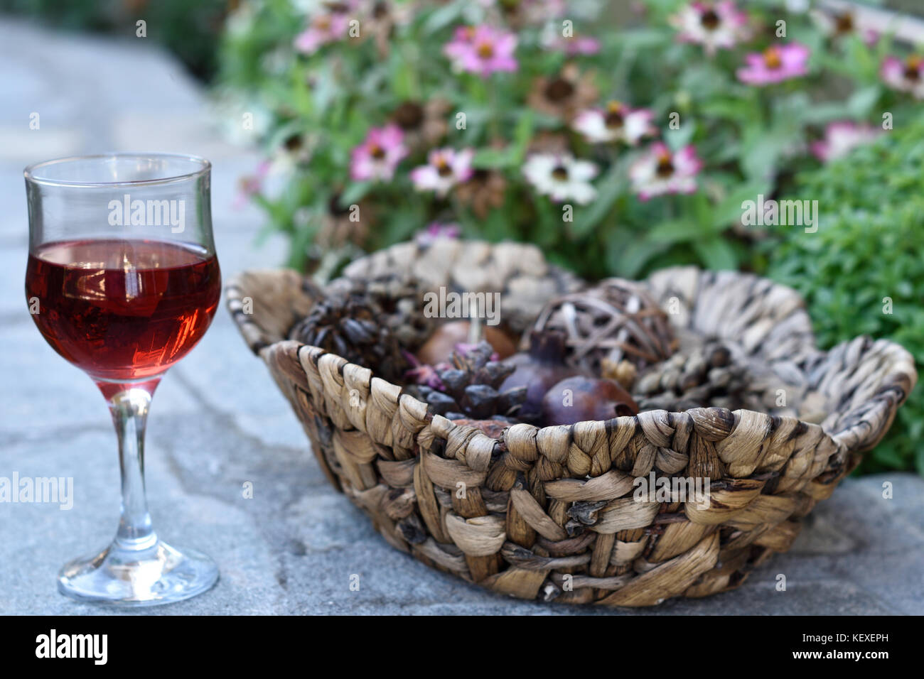 Glass of red vine standing on a stone wall next to a basket of dried ...