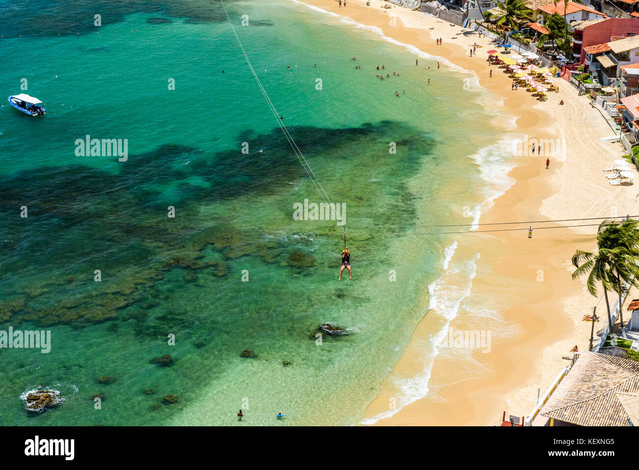 Photograph of adventurous person riding zip line above tropical beach ...
