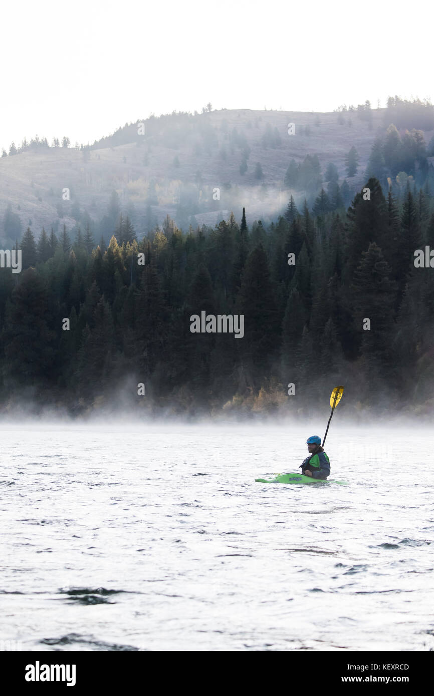 Person kayaking on Snake River against forested hills during foggy ...