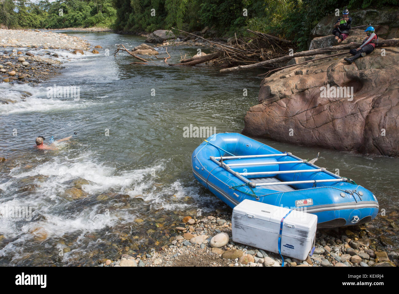 Photograph of inflatable raft, cooler and two men on riverbank before ...